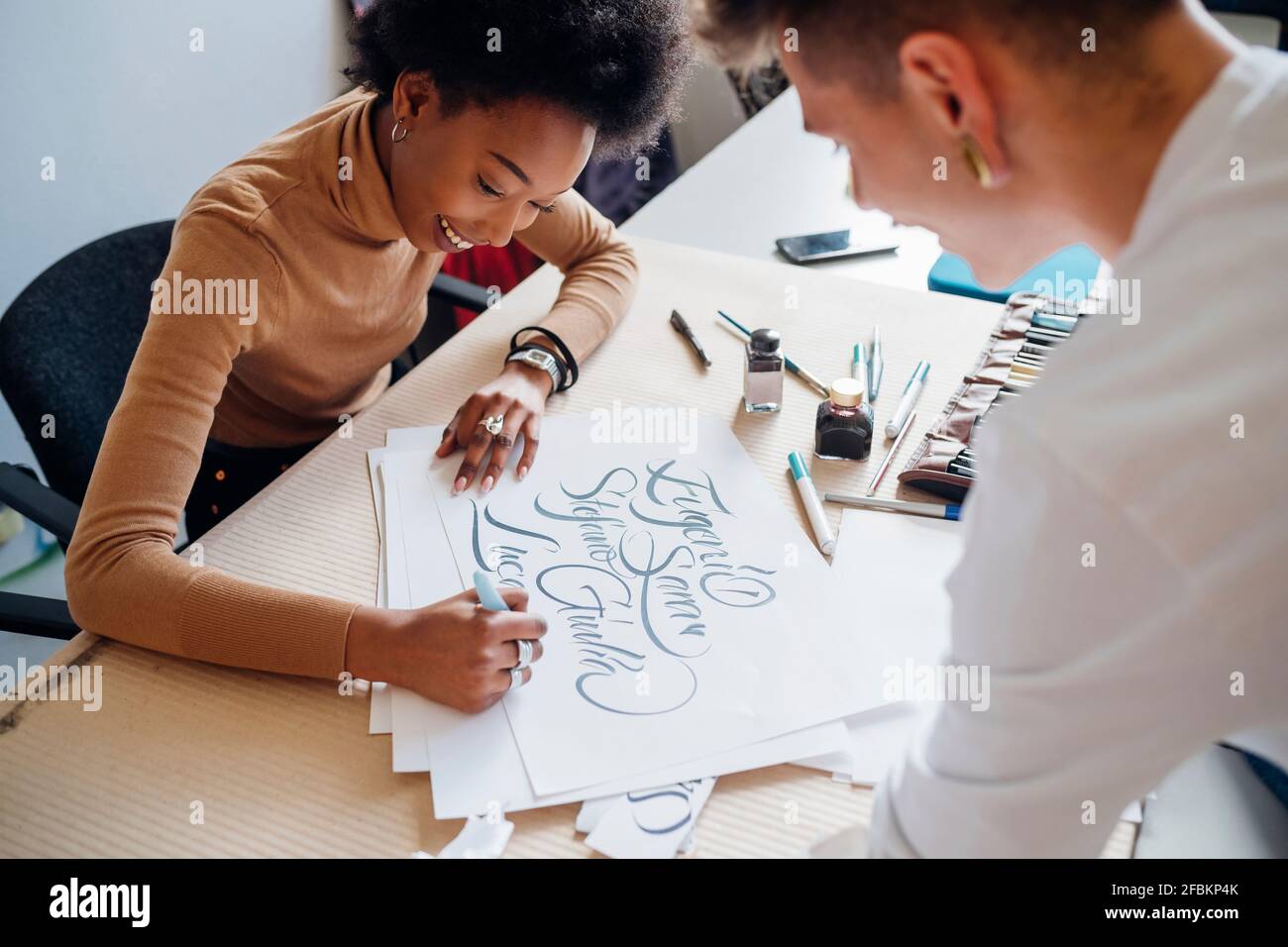 Smiling African woman writing calligraphy on paper while sitting with ...