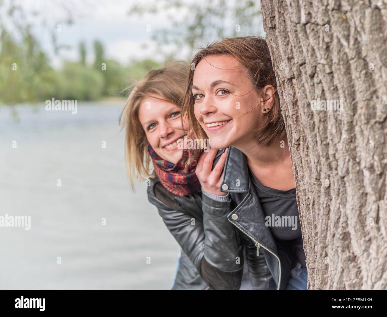 Portrait of two friends hiding behind tree trunk Stock Photo - Alamy