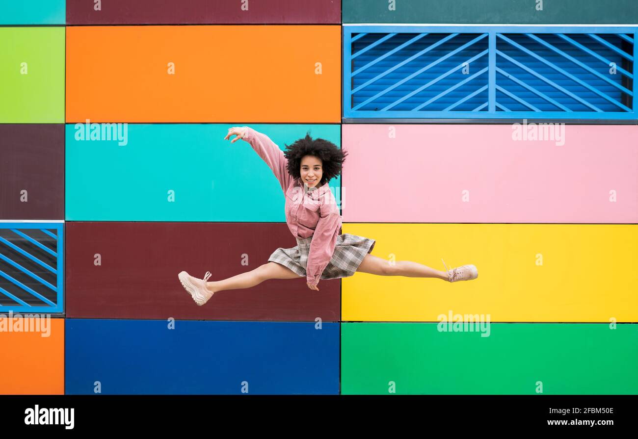 Female dancer jumping with leg splits in front of multi colored wall ...