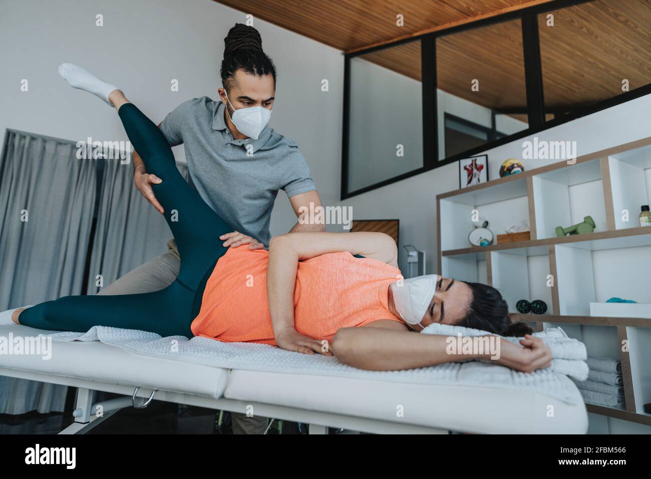 Male medical professional wearing face mask stretching leg of patient ...