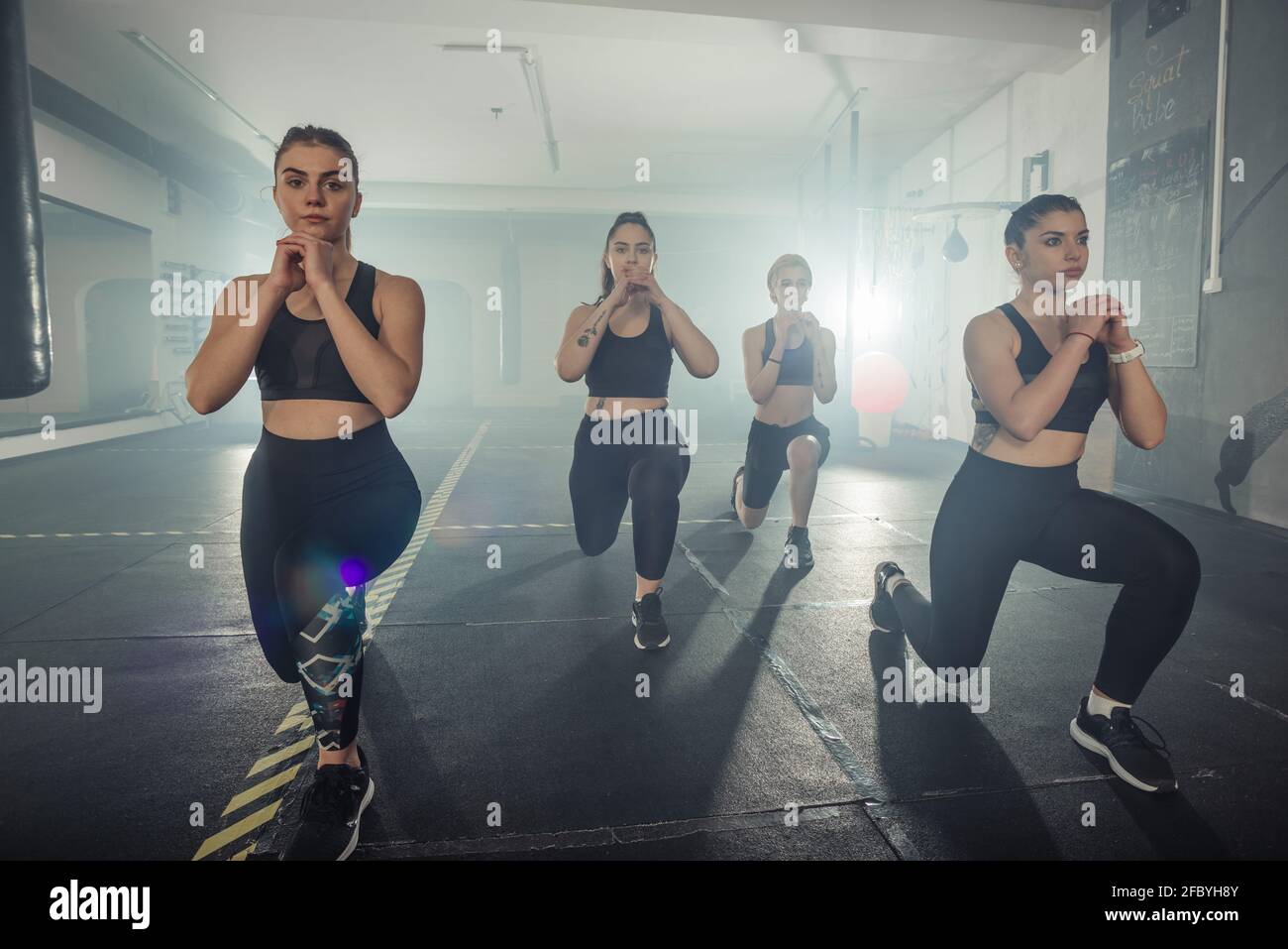 Group of sportswomen in sportswear doing lunge exercise at the gym with ...