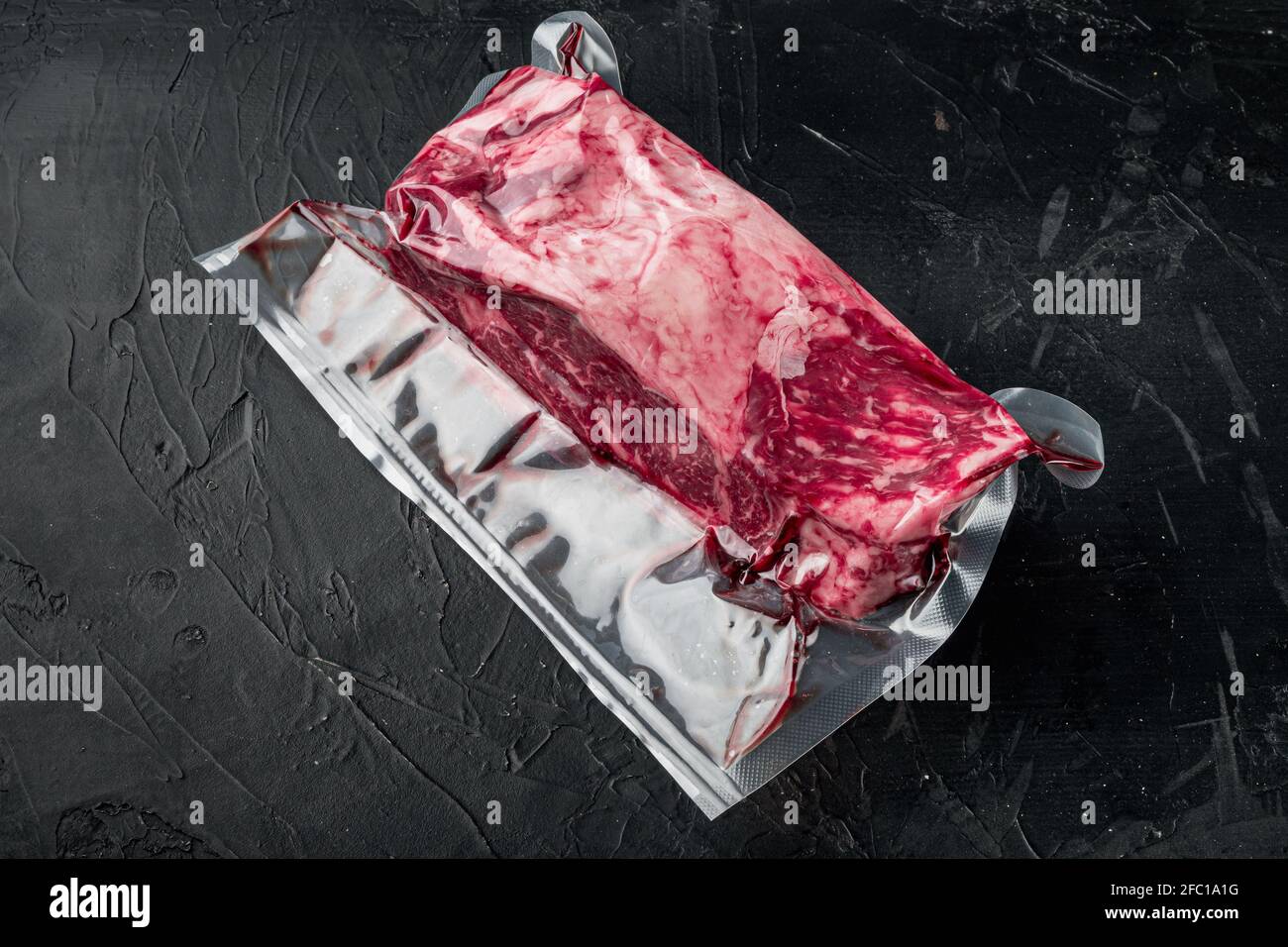 Fresh premium rib eye whole cut in a vacuum pack package set, on black ...