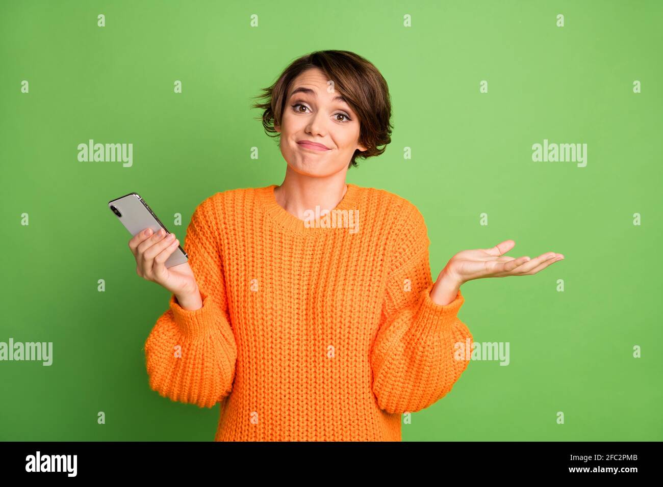 Photo of uncertain young woman shrug shoulders hold smartphone blogger ...
