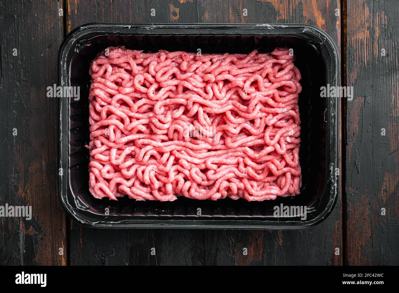 Ground beef meat in plastic tray set, on old dark wooden table ...