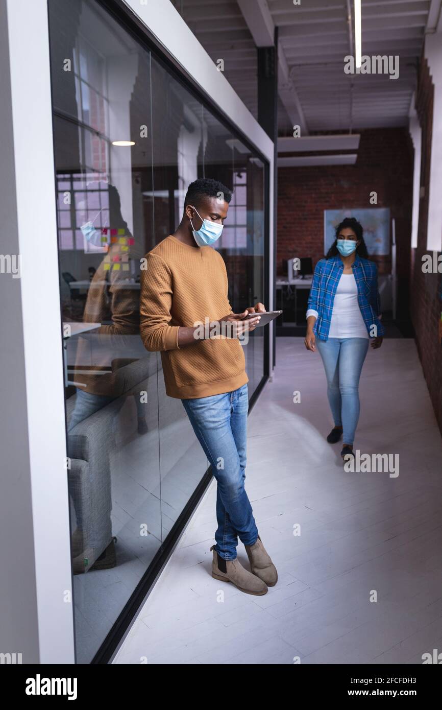 Diverse male and female colleagues wearing face mask standing in ...