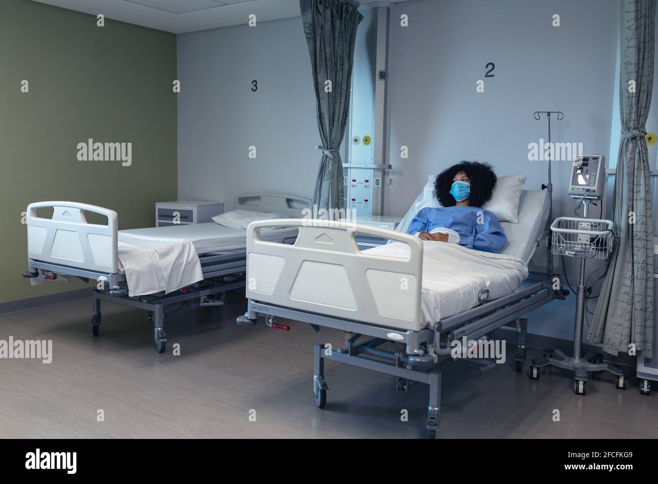 African american female patient lying in hospital bed wearing face mask ...