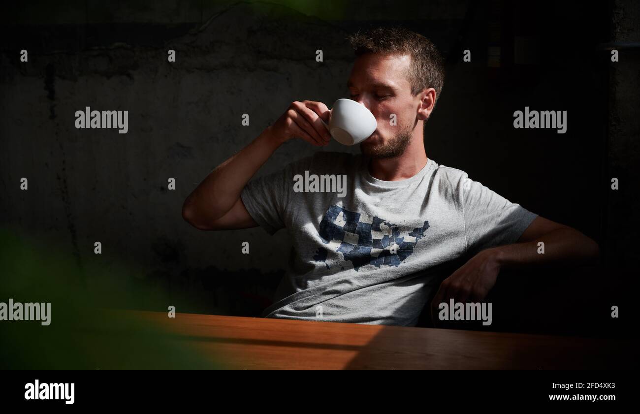 Male resting with cup of coffee in cafe. Young man sitting by desk and ...