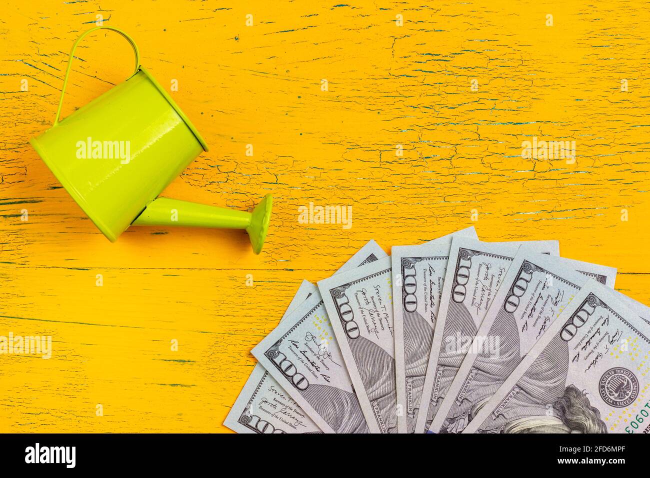 Small garden watering can and dollar bills on a yellow background ...