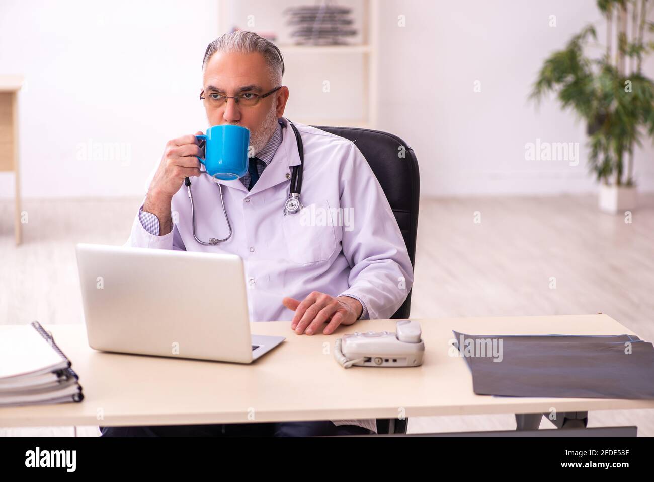 Aged male doctor drinking coffee at workplace Stock Photo - Alamy