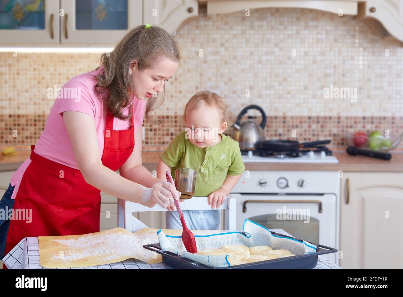 A young woman teaches a child to cook pastries. Greases the pies in the ...