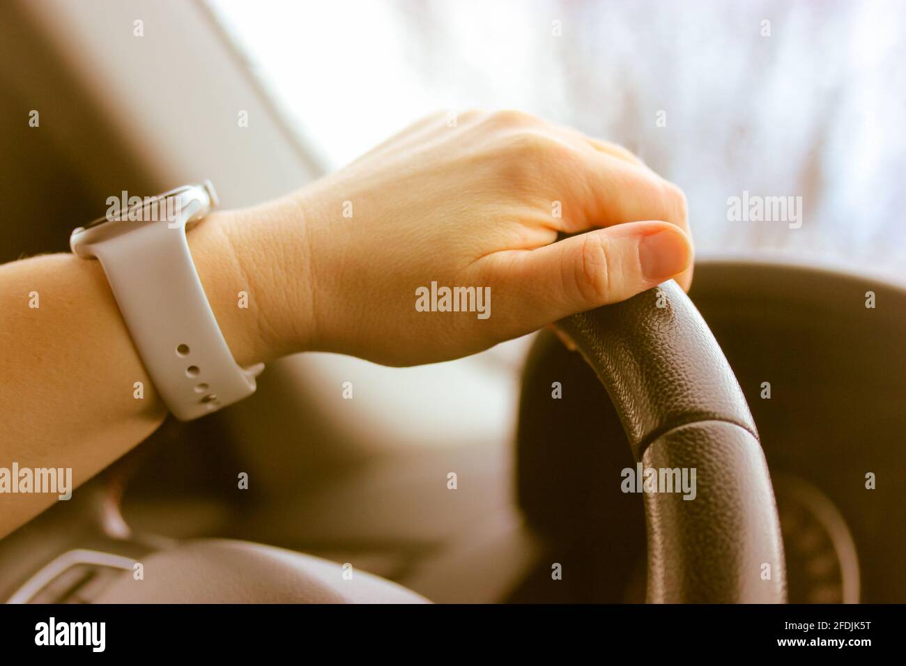 A woman's hand with a white watch is holding a black car steering wheel ...