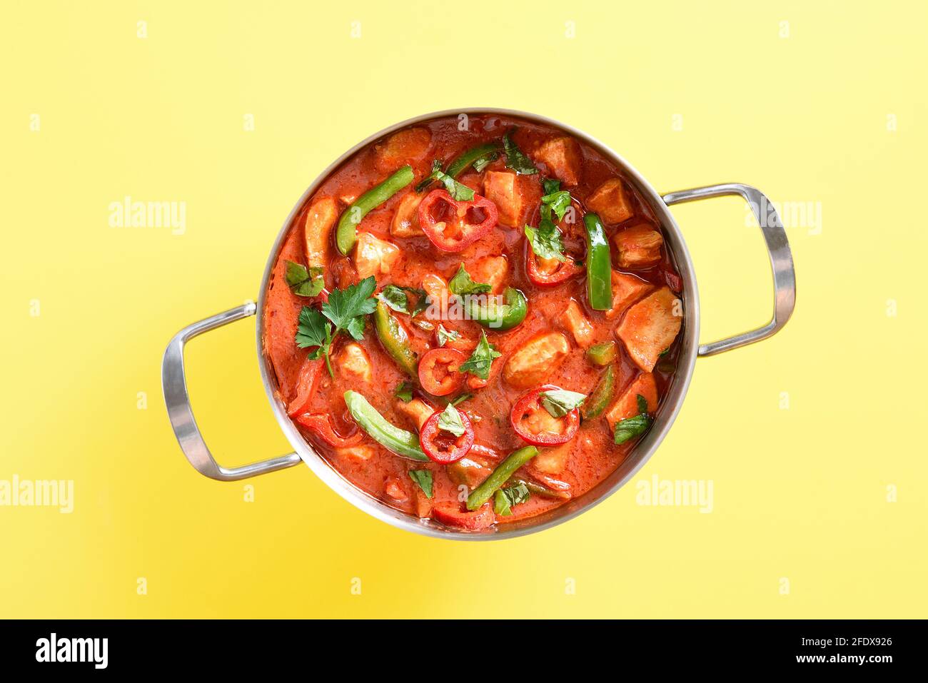 Thai style red chicken curry with vegetables in pan over yellow ...