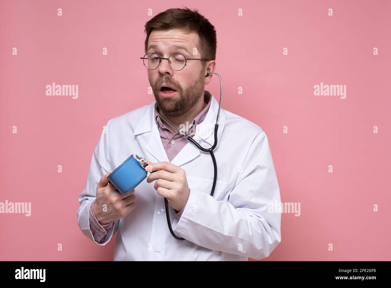 Sleepy doctor with glasses holds a mug of coffee and listens to it with ...
