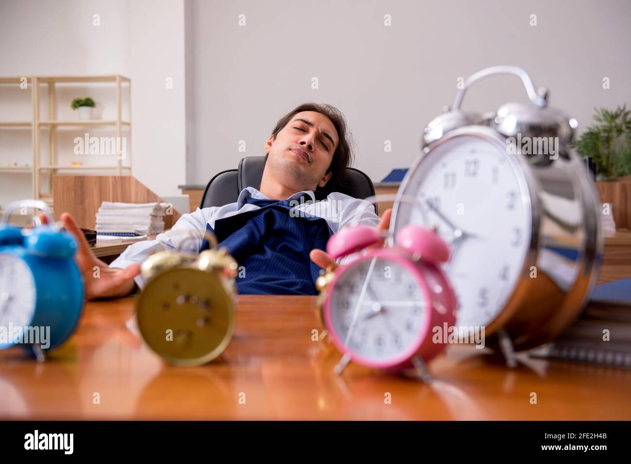 Young businessman sleeping in the office in time management concept ...