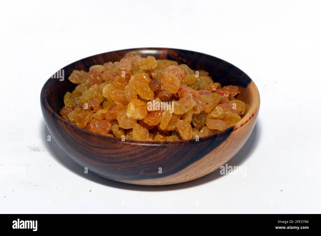 Dried raisins in a brown wooden bowl isolated on a white background ...