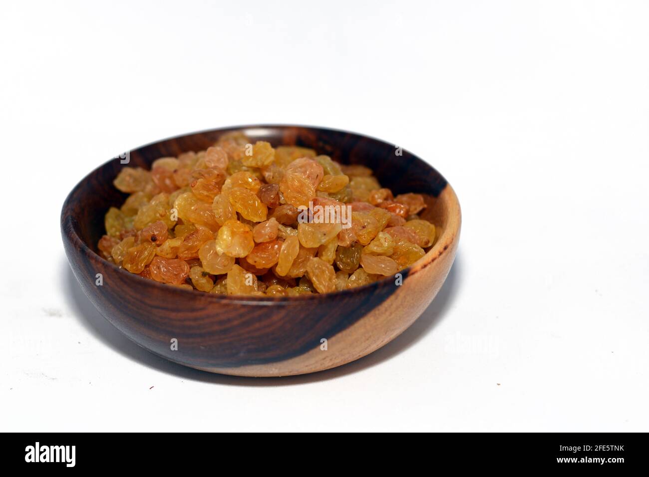 Dried raisins in a brown wooden bowl isolated on a white background ...
