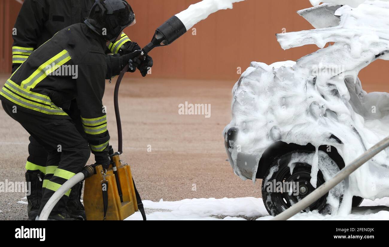 firefighters extinguishes a fire while a crashed car with the foaming ...
