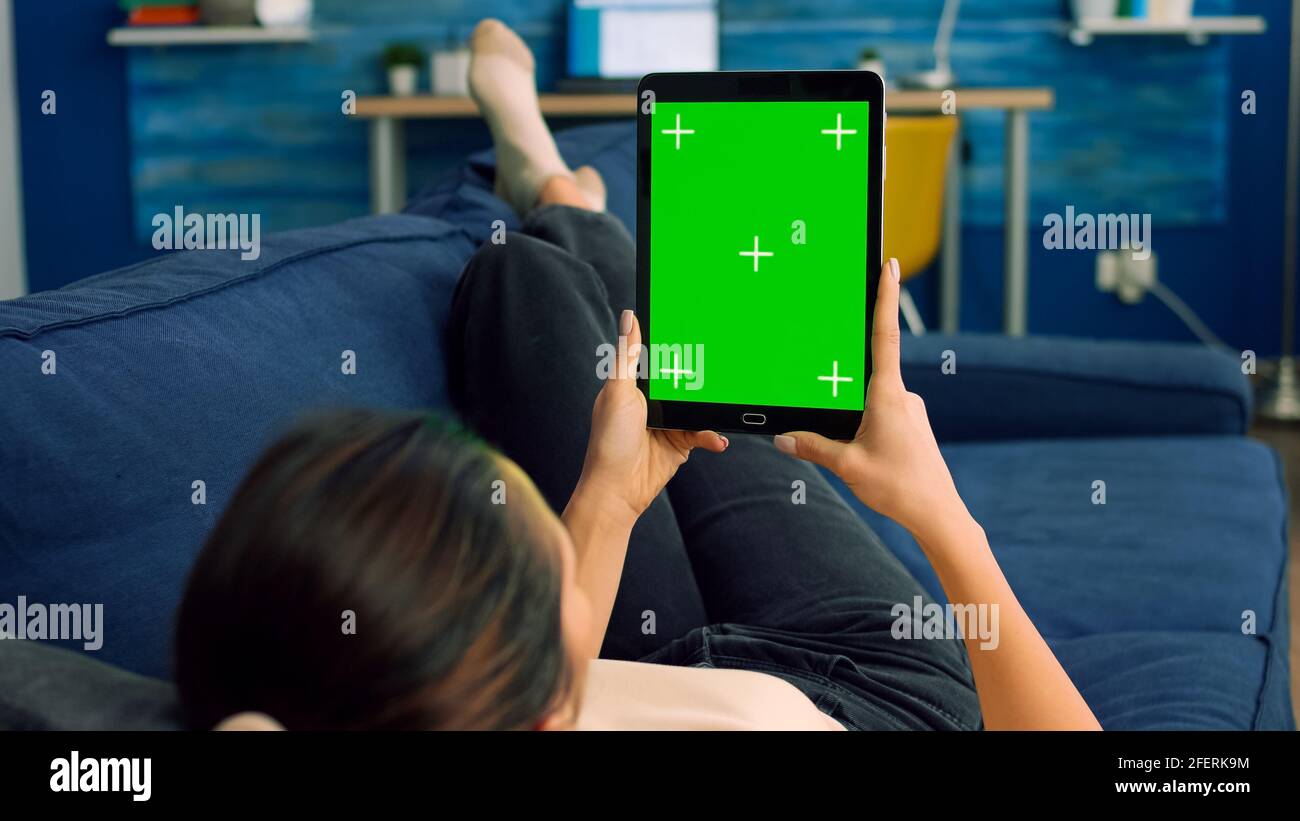 Casual woman lying on sofa using tablet computer mock up green screen chroma key in vertical ...