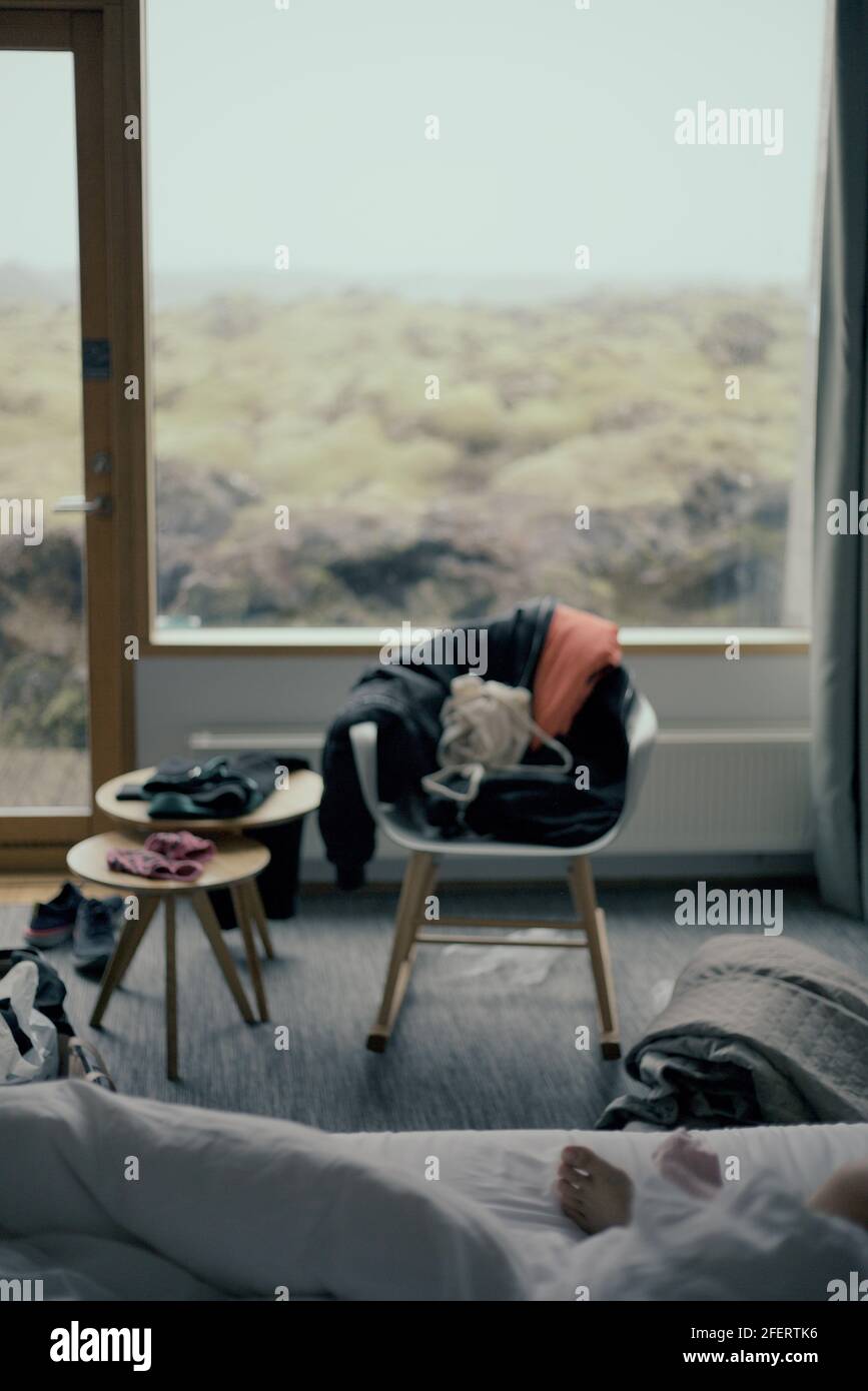 Vertical shot of small wooden stools and a messy bed in a room with big ...
