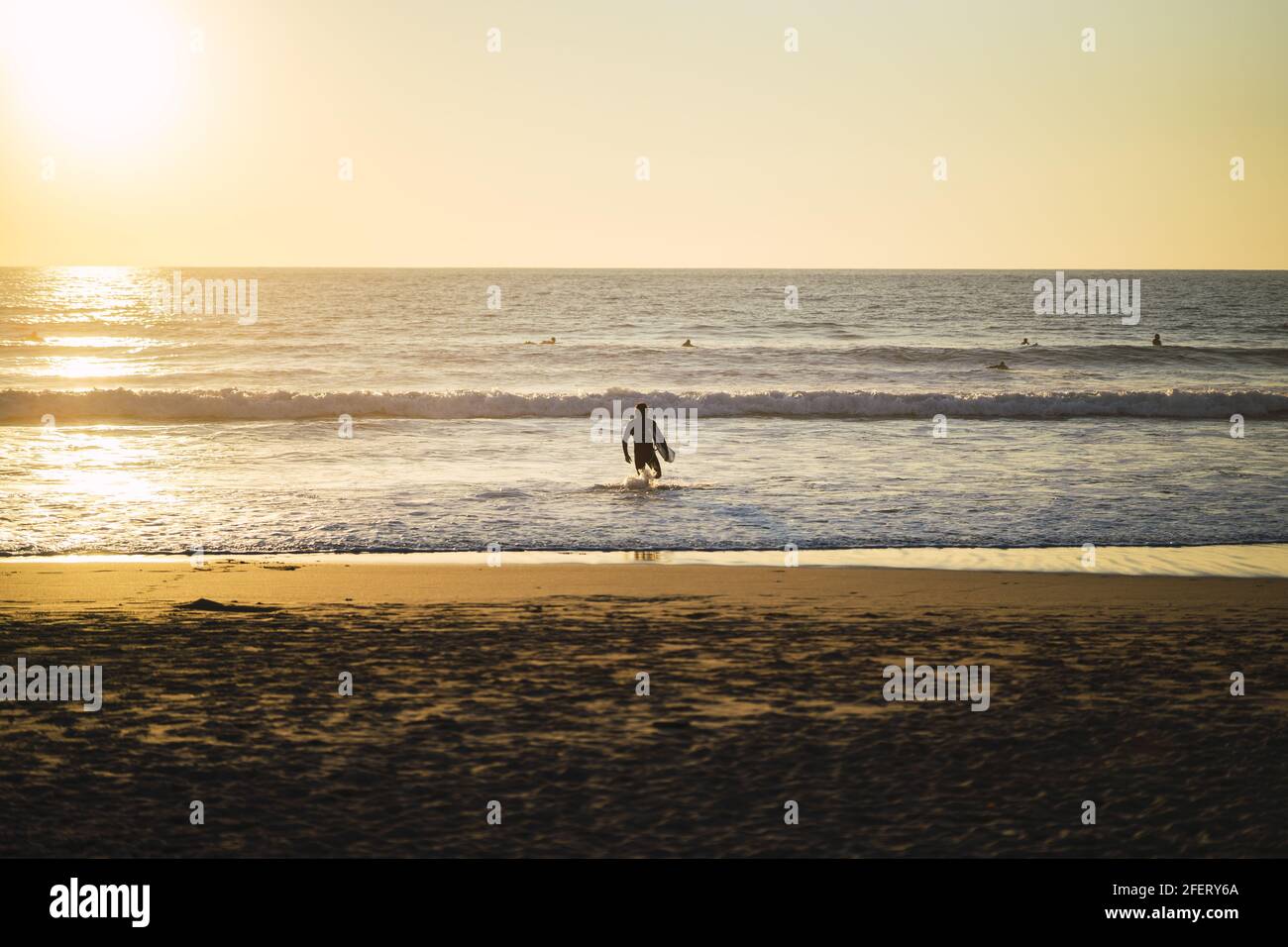 Surfer running into the water on a beach during a beautiful sunset ...