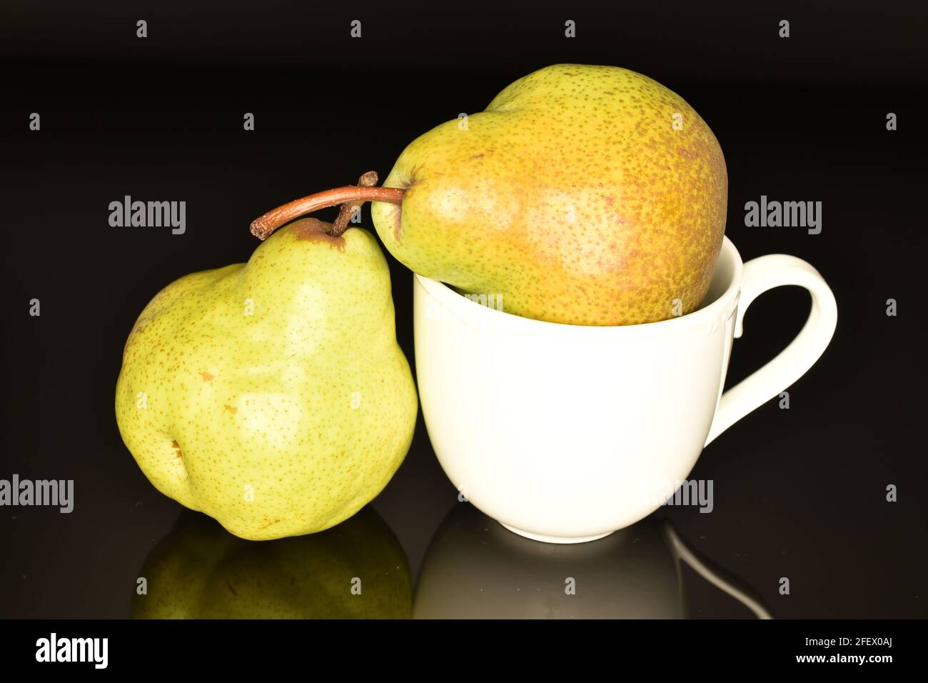 Two natural pears with a white cup, close-up, on a black background ...