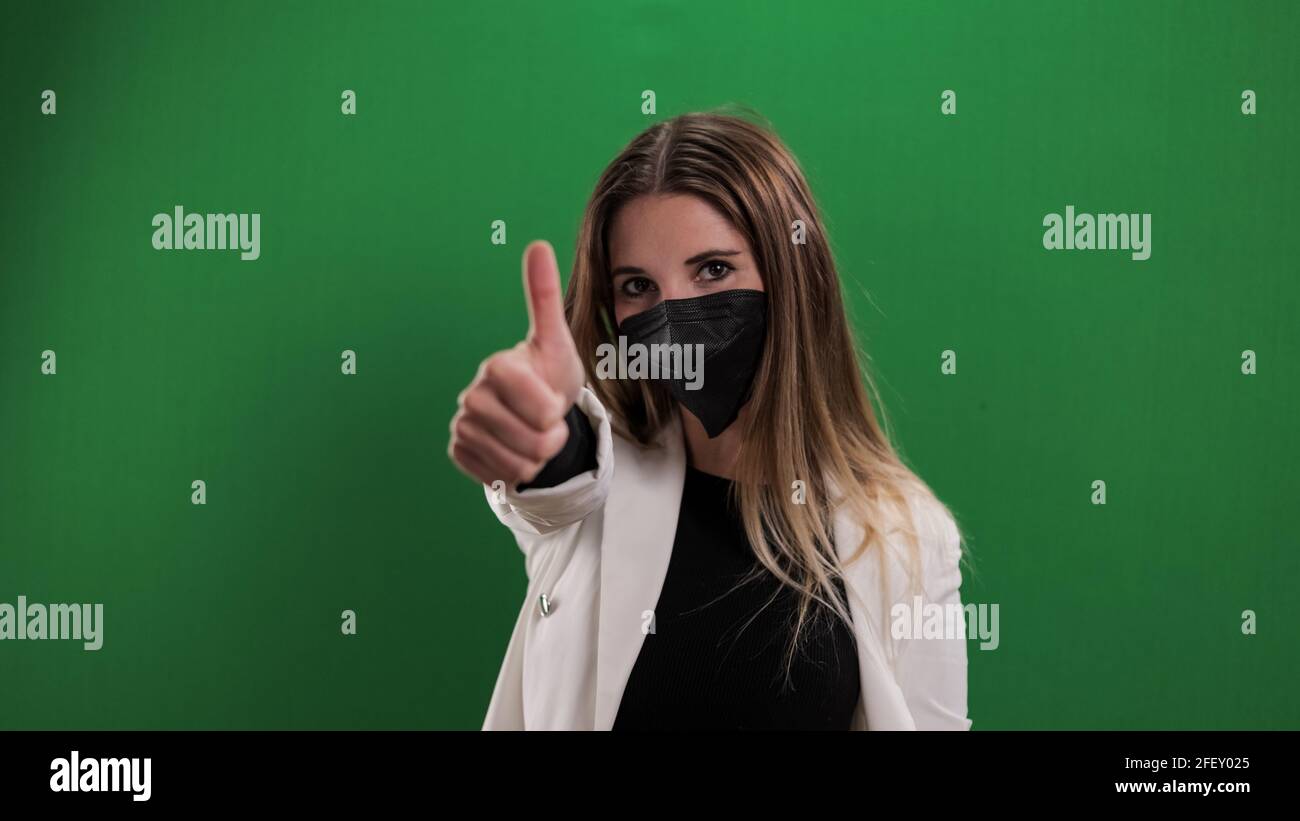 Young woman wearing face mask makes thumbs up gesture Stock Photo - Alamy