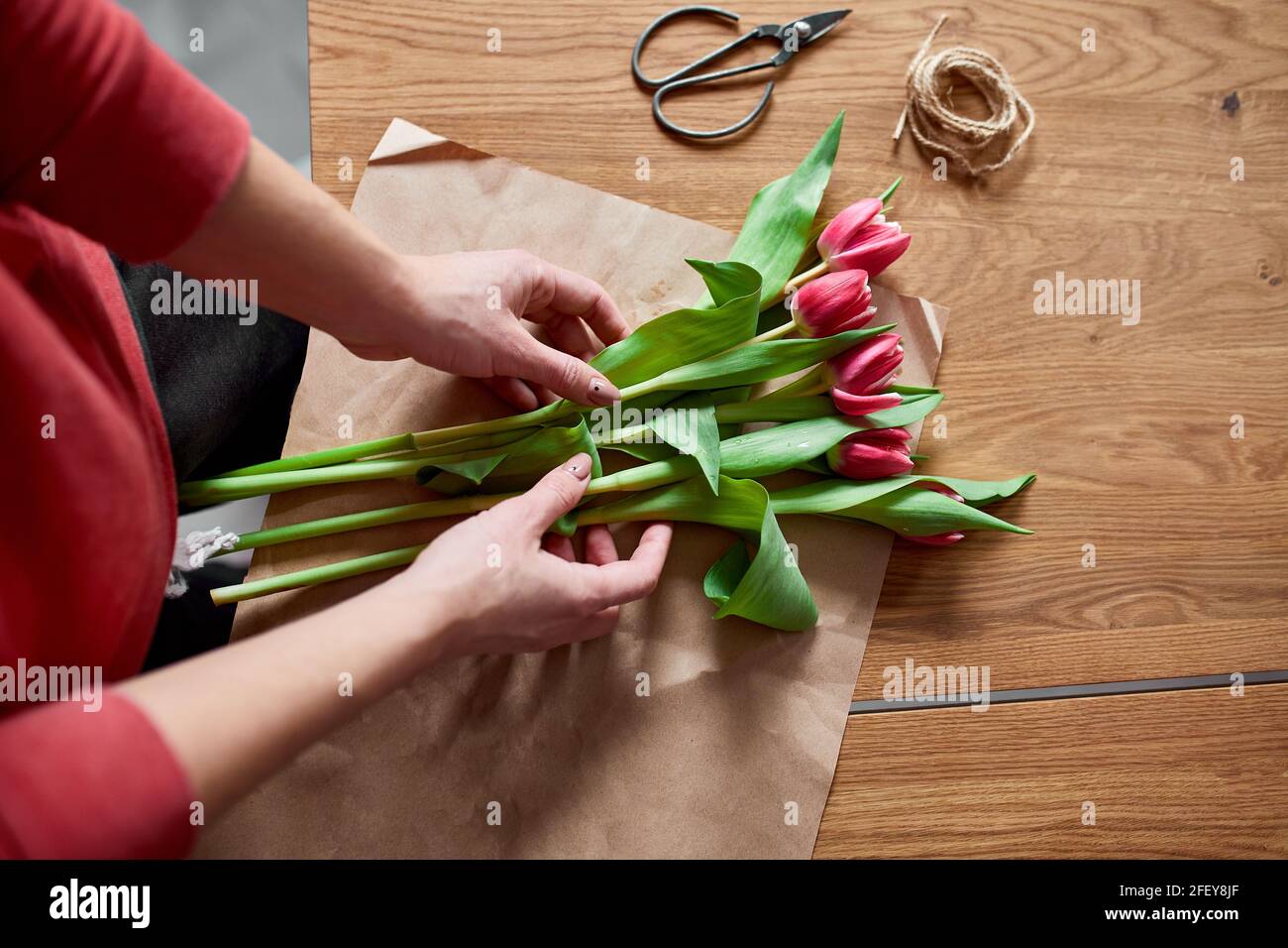 Female hands arranging pink tulips bouquet on wooden table, floristic ...