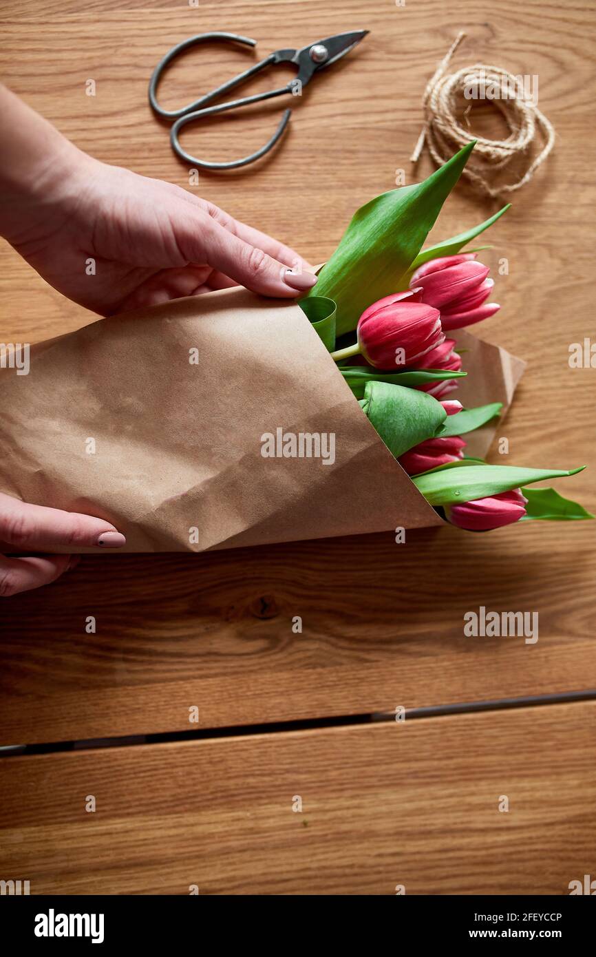 Female hands arranging pink tulips bouquet on wooden table, floristic ...