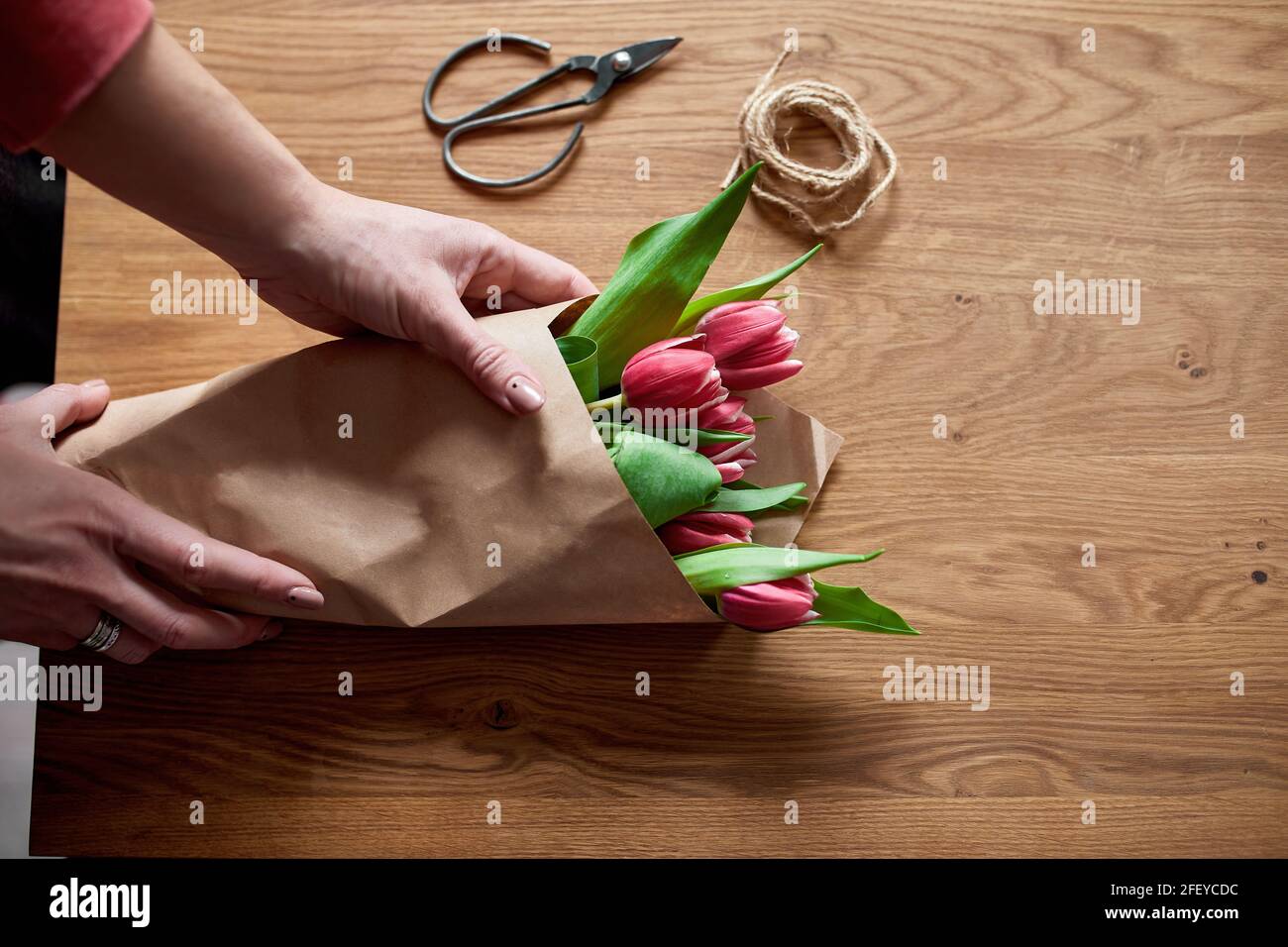 Female hands arranging pink tulips bouquet on wooden table, floristic ...