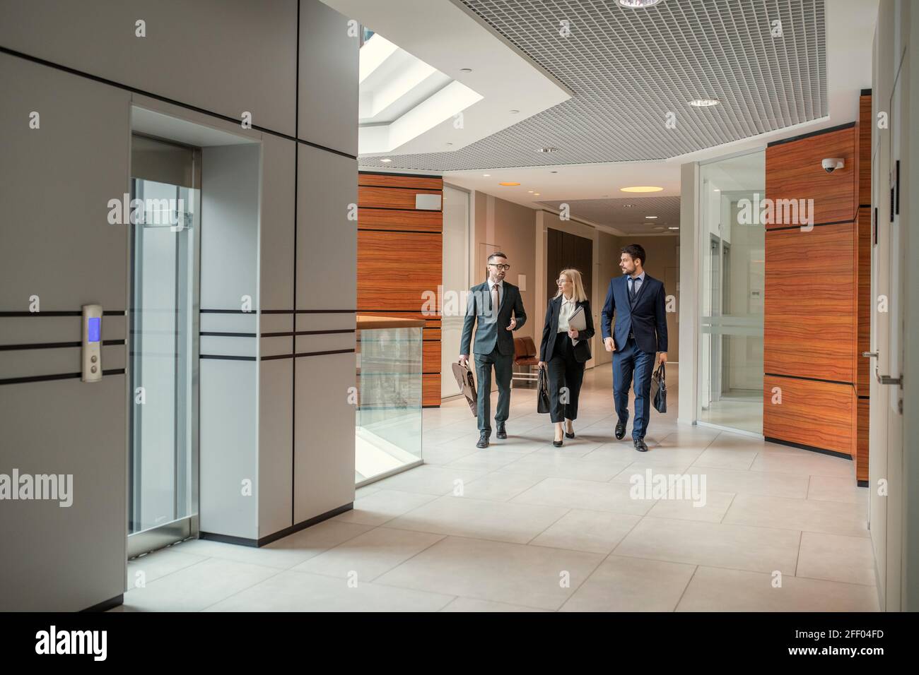 Modern business colleagues of different ages walking in corridor and ...