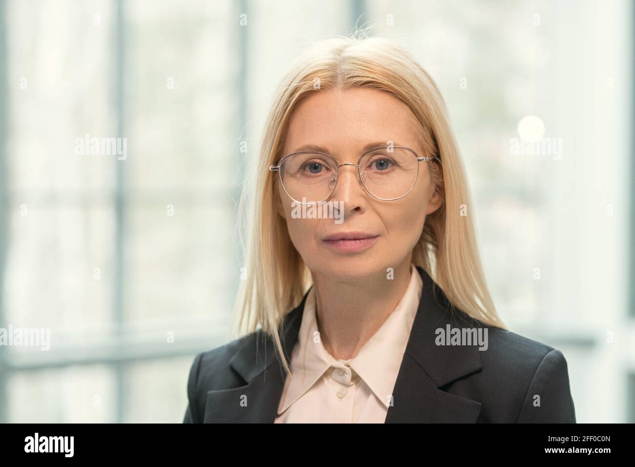 Portrait of serious beautiful mature executive in round glasses ...