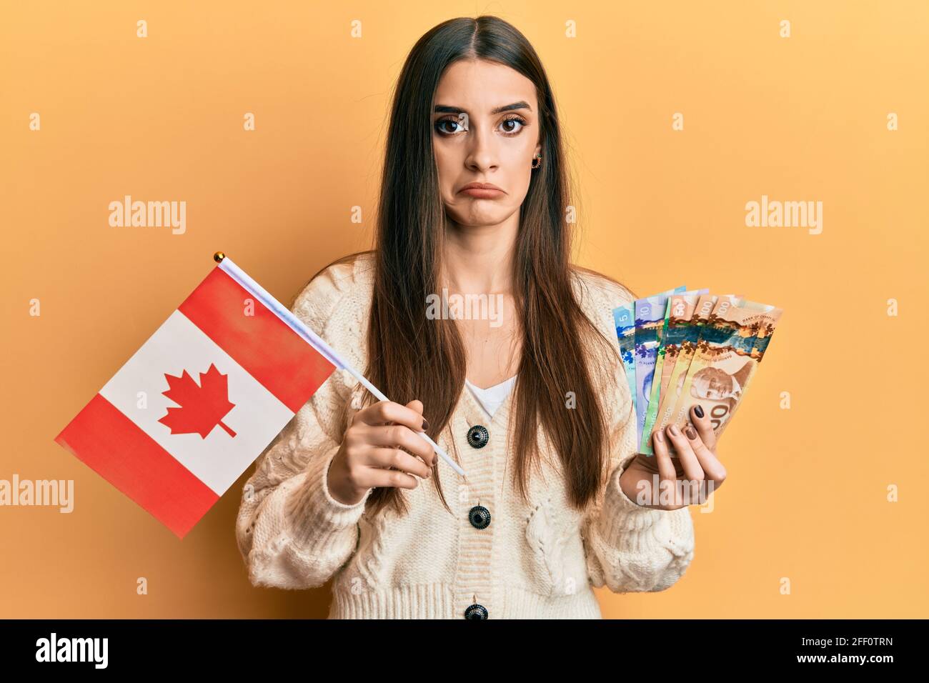 Beautiful brunette young woman holding canada flag and dollars ...