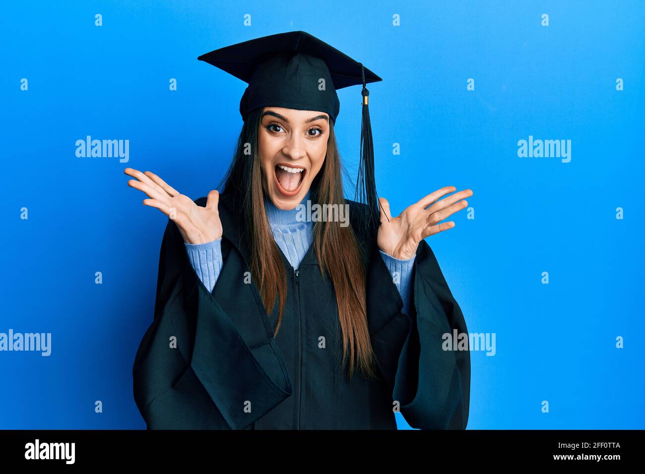 Beautiful brunette young woman wearing graduation cap and ceremony robe ...
