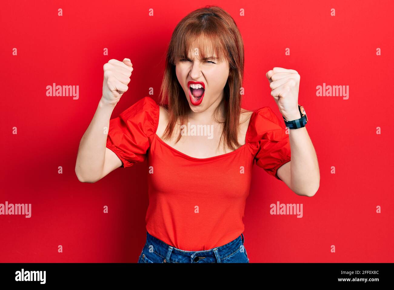 Redhead young woman wearing casual red t shirt angry and mad raising ...