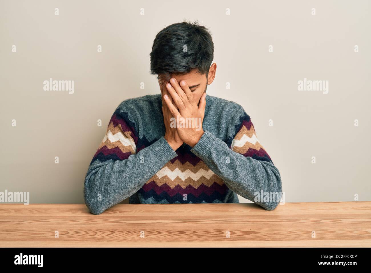 Young handsome man wearing casual sweater sitting on the table with sad ...