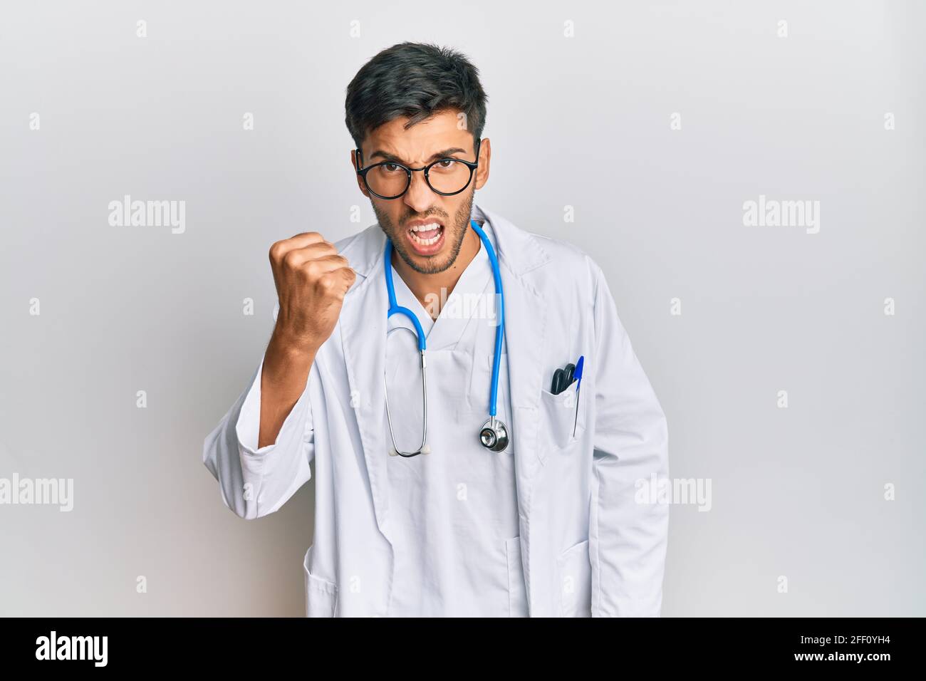Young handsome man wearing doctor uniform and stethoscope angry and mad ...