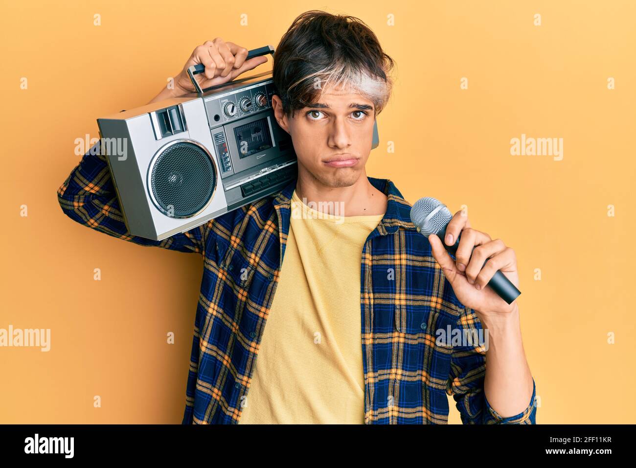 Young hispanic man singing song using microphone and boombox depressed ...