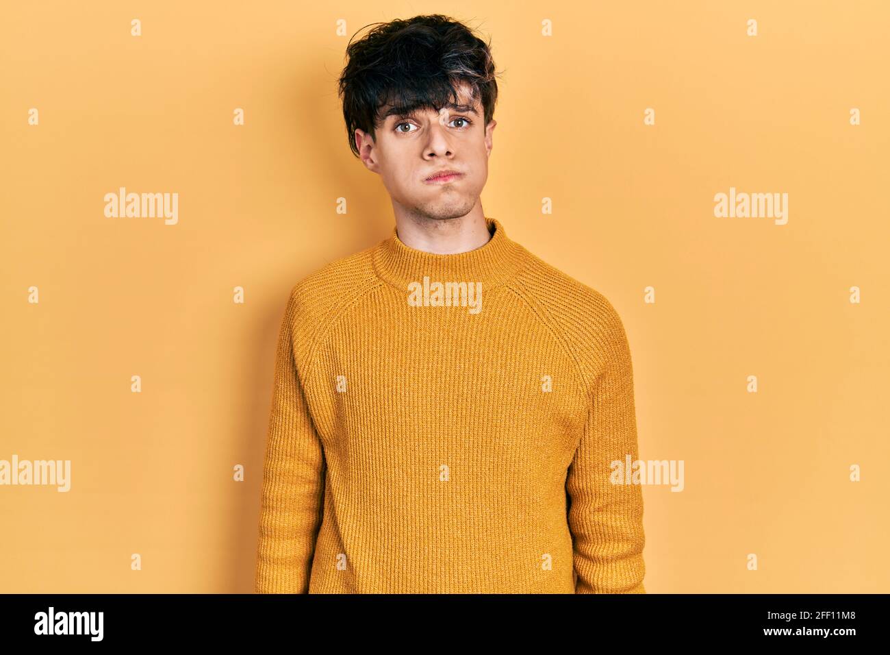 Handsome hipster young man wearing casual yellow sweater puffing cheeks ...