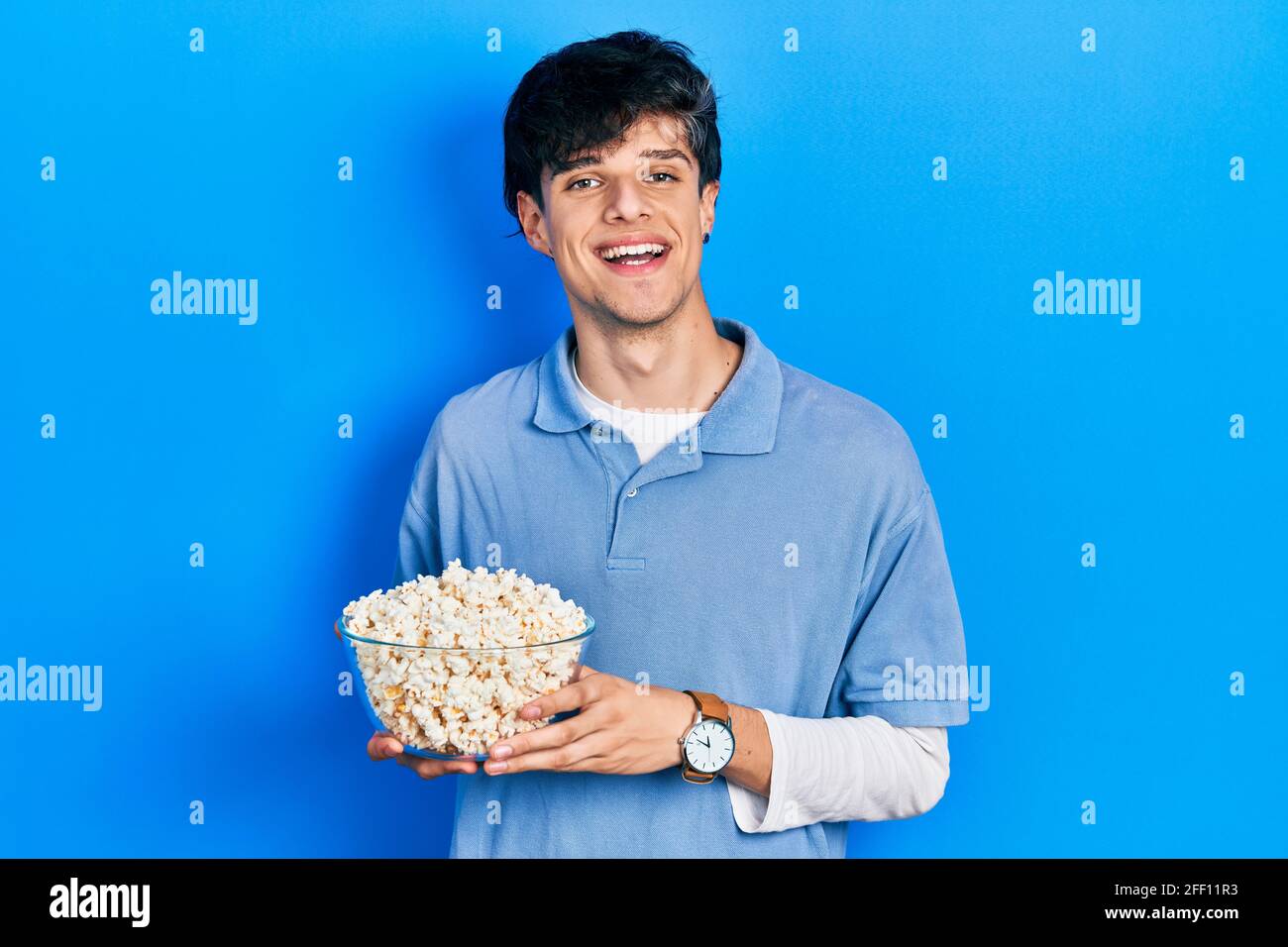 Handsome hipster young man eating popcorn looking positive and happy ...