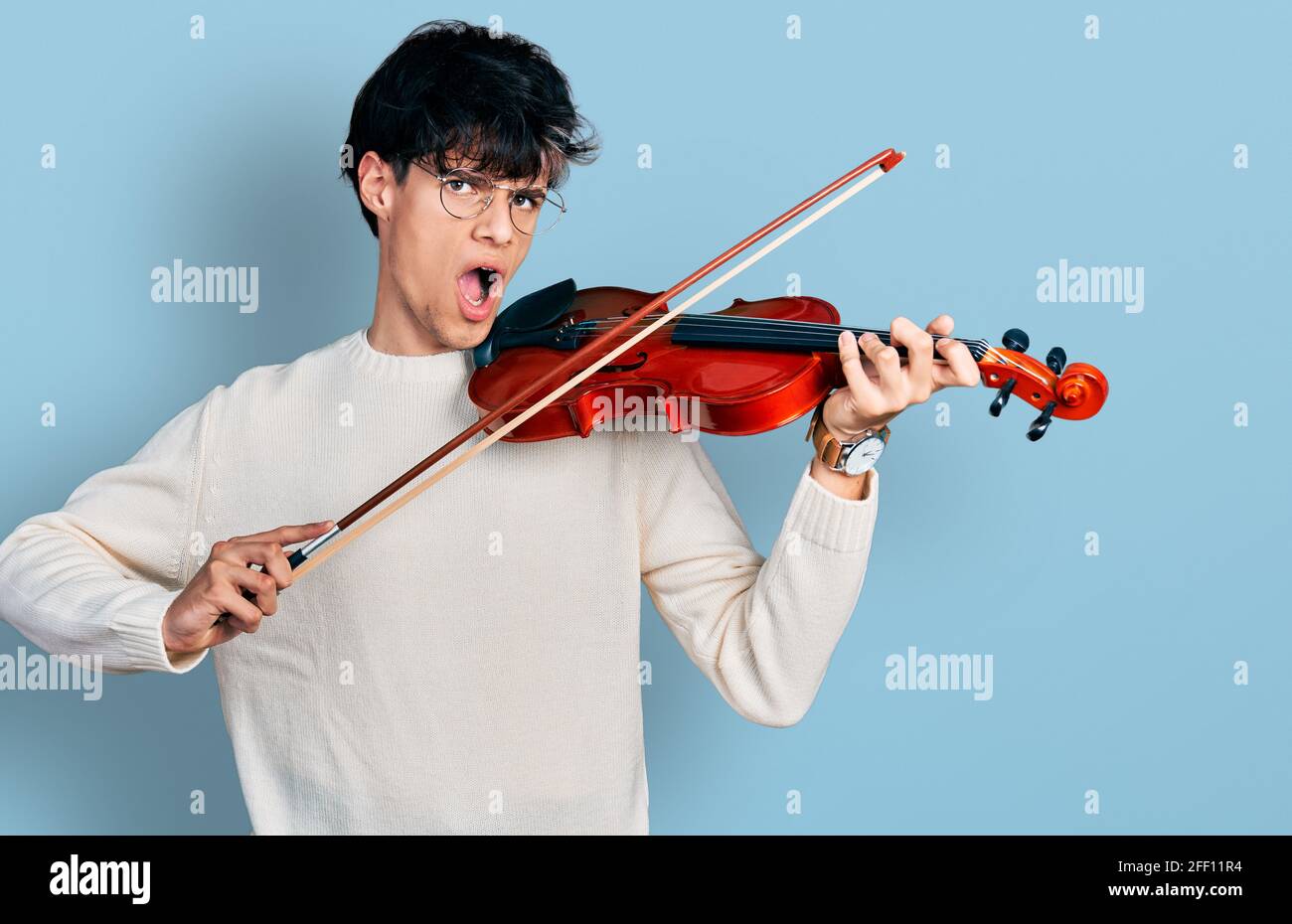 Handsome hipster young man playing violin in shock face, looking ...