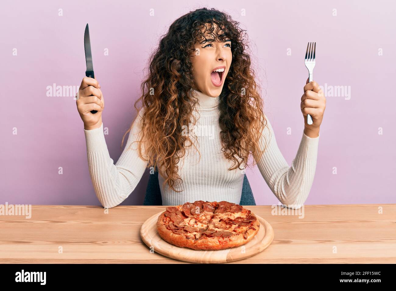Young hispanic girl eating tasty pepperoni pizza angry and mad ...