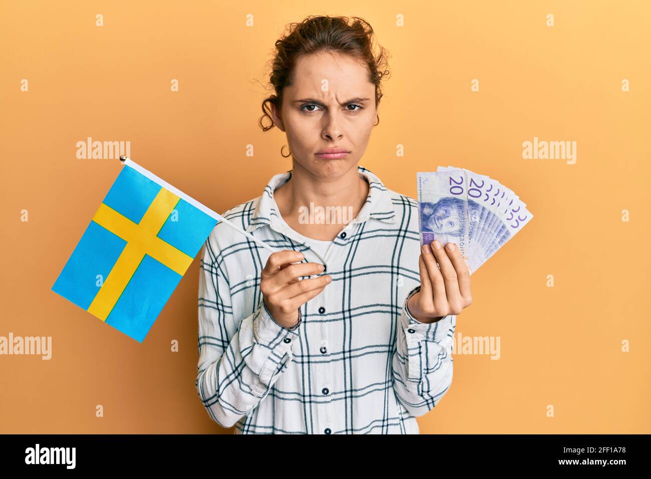 Young brunette woman holding sweden flag and krone banknotes depressed ...