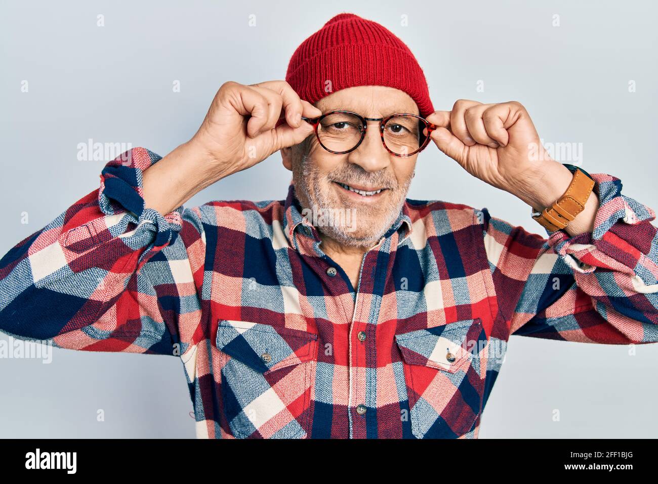 Handsome mature man holding glasses, wearing wool hat smiling with a ...