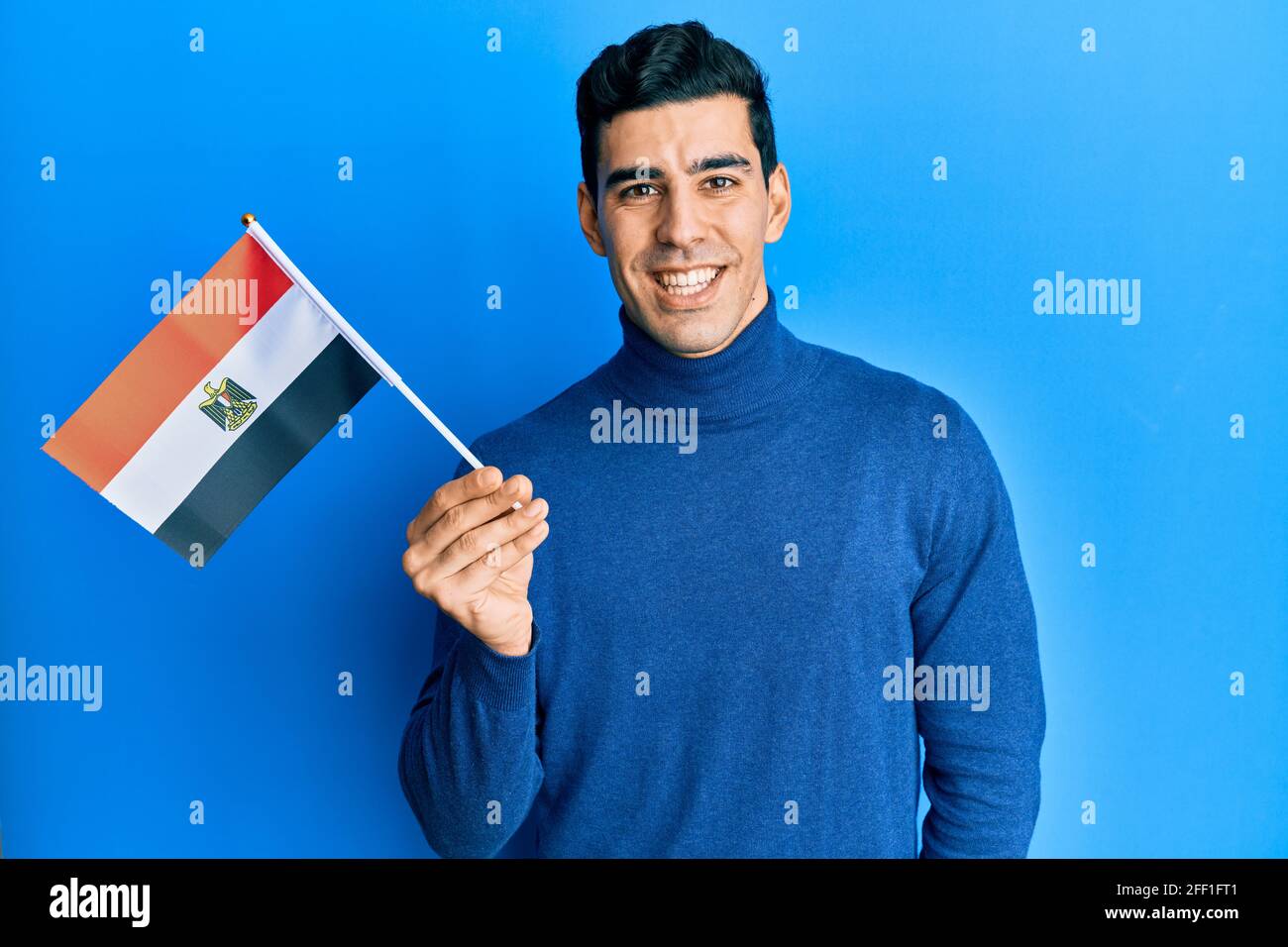 Handsome hispanic man holding egypt flag looking positive and happy ...