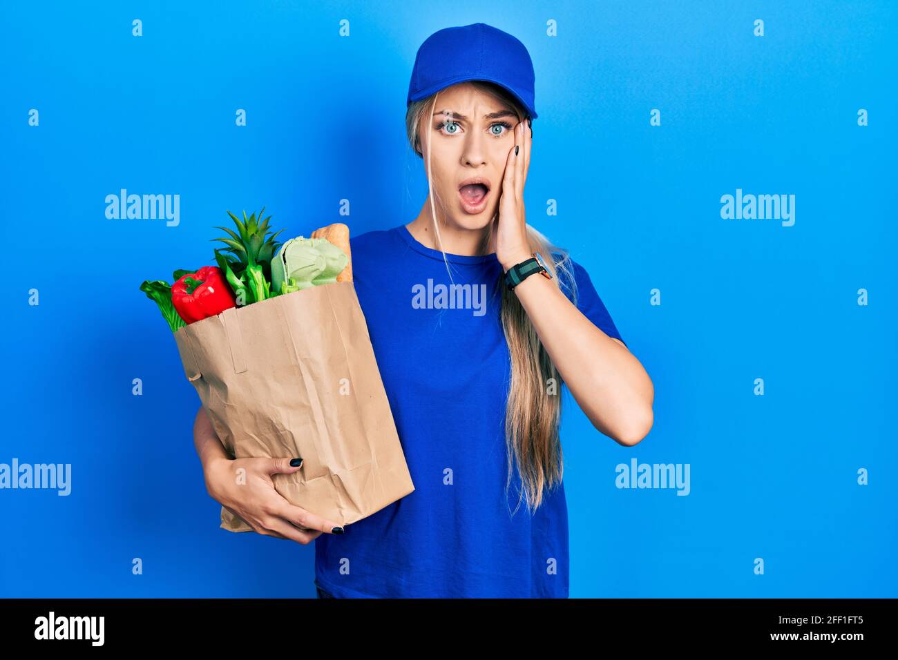 Young caucasian woman wearing courier uniform with groceries from ...