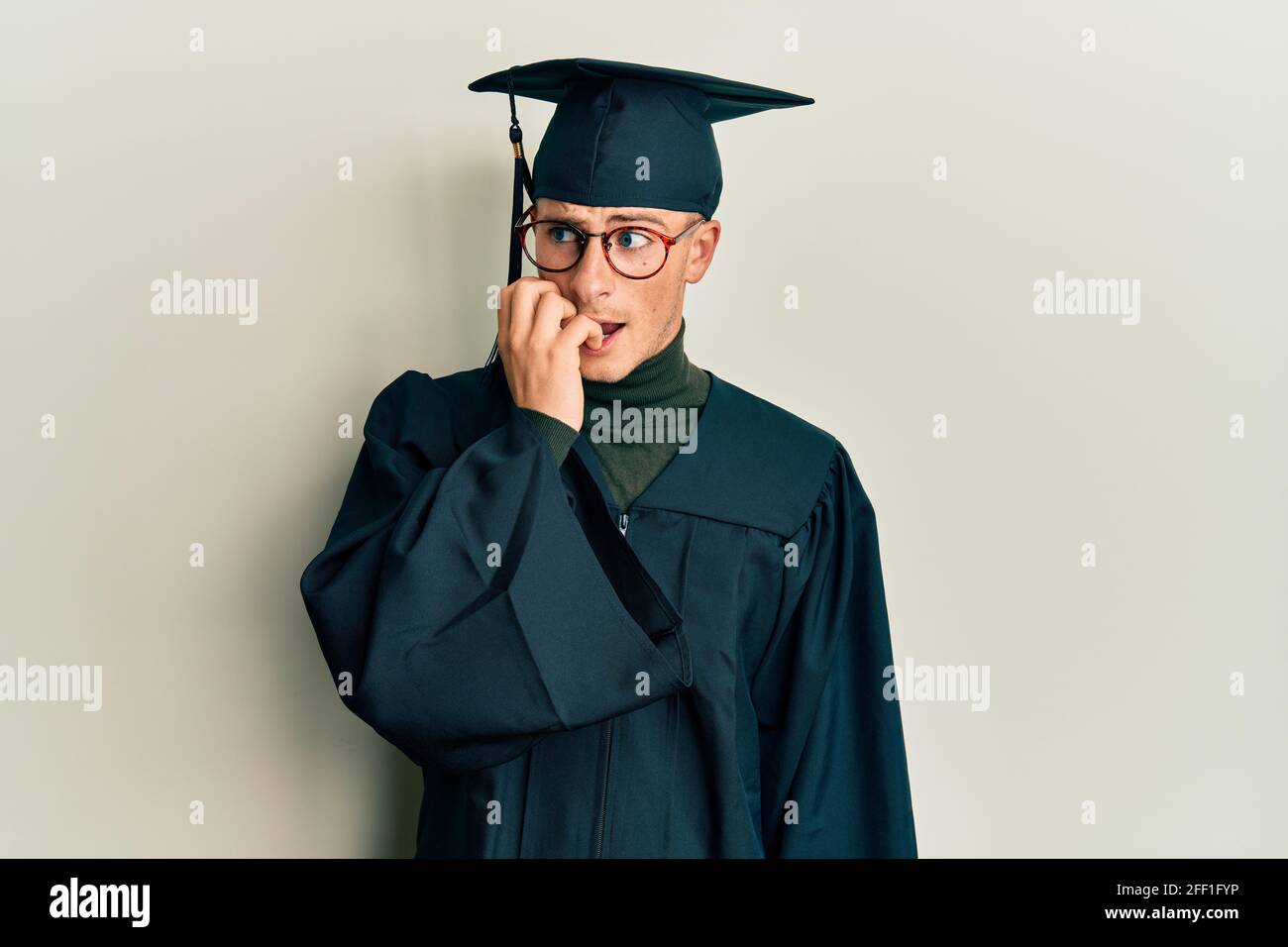 Young caucasian man wearing graduation cap and ceremony robe looking ...