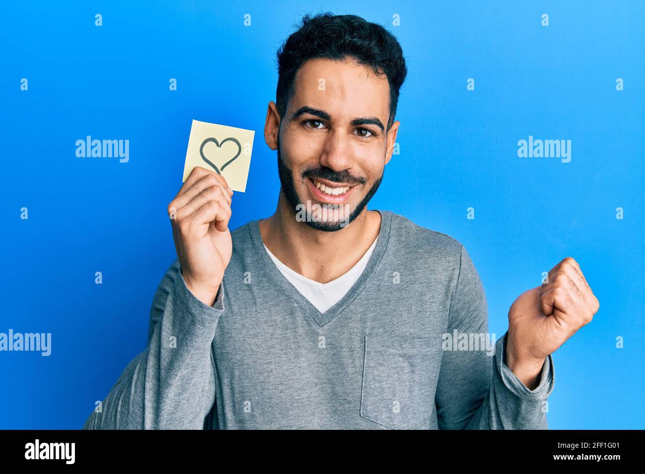 Young hispanic man holding heart reminder screaming proud, celebrating ...