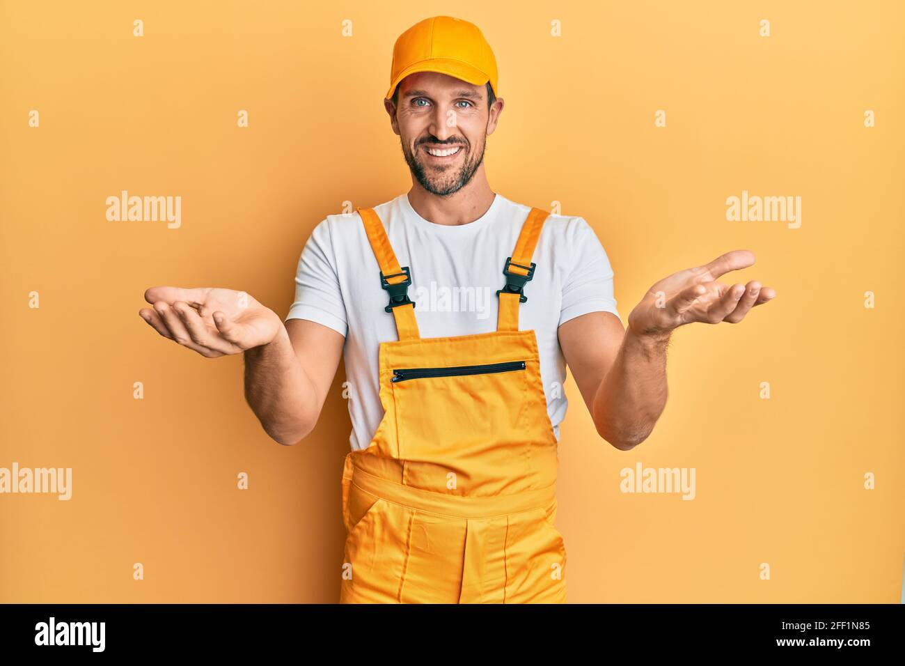 Young handsome man wearing handyman uniform over yellow background ...