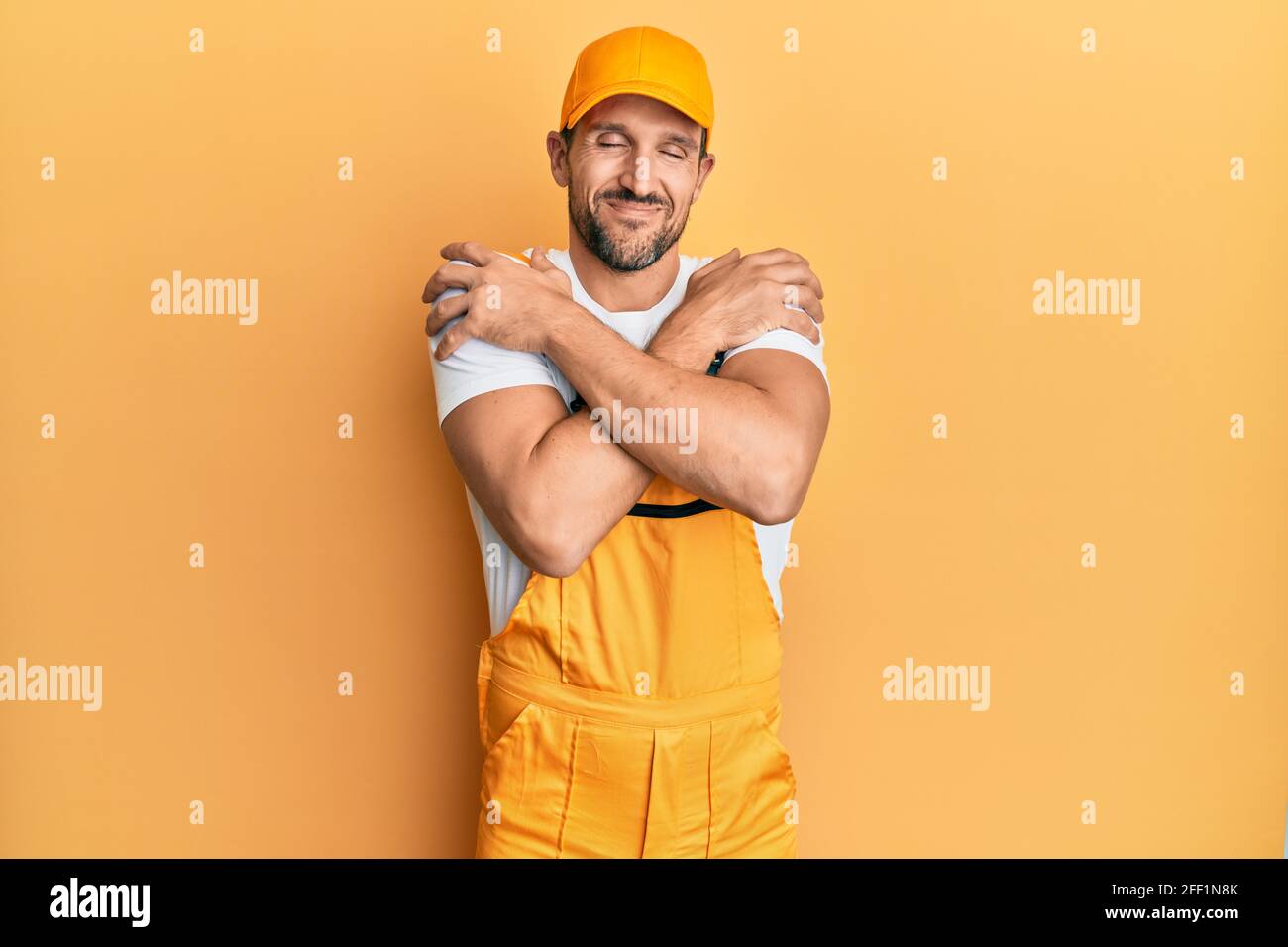Young handsome man wearing handyman uniform over yellow background ...