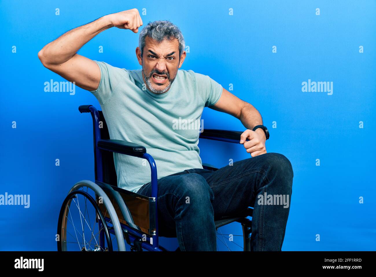 Handsome middle age man with grey hair sitting on wheelchair angry and ...